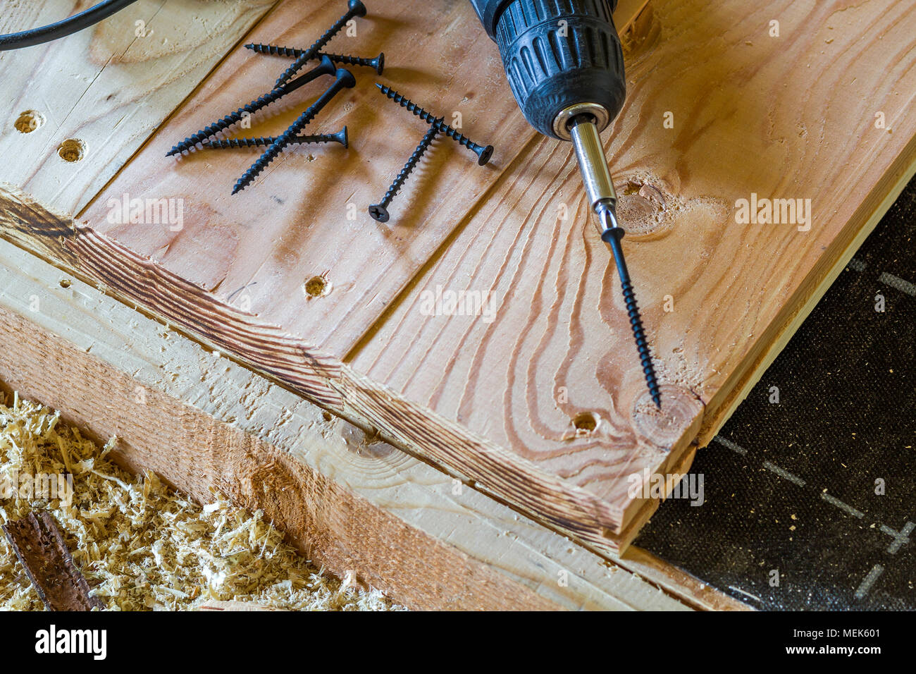 Close up of electric screwdriver with some screws laying on old rough ...