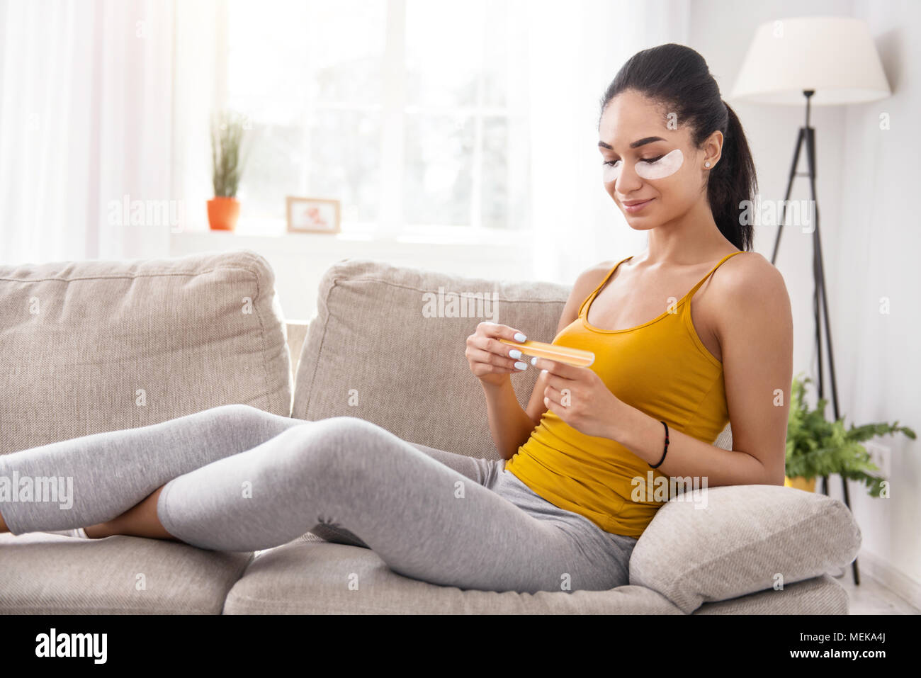 Pretty young woman filing her nails on couch Stock Photo - Alamy