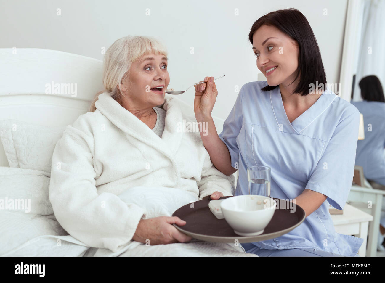 Joyful caregiver giving breakfast to elder woman Stock Photo - Alamy