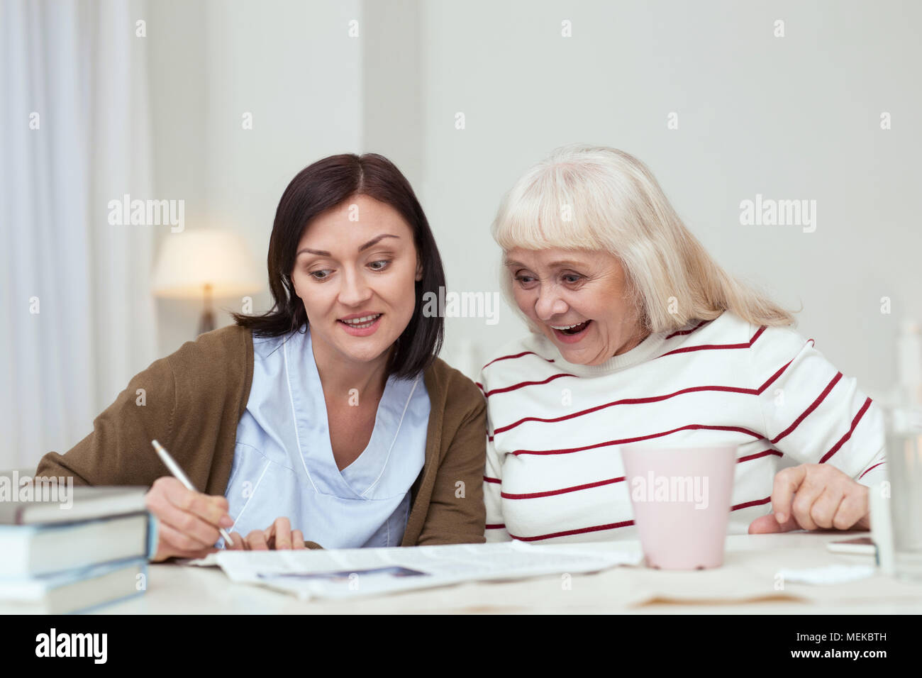 Active elder woman and caregiver viewing newspaper Stock Photo - Alamy