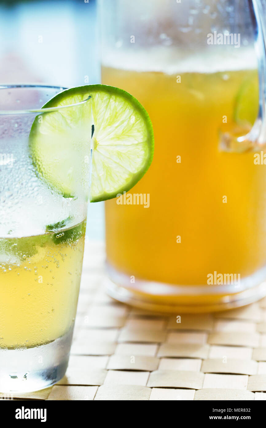 Yellow coloured drink with lime slice and jug of drink Stock Photo - Alamy