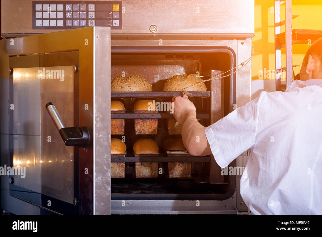 A male baker in white uniform and a beige apron bakes bread from an ...