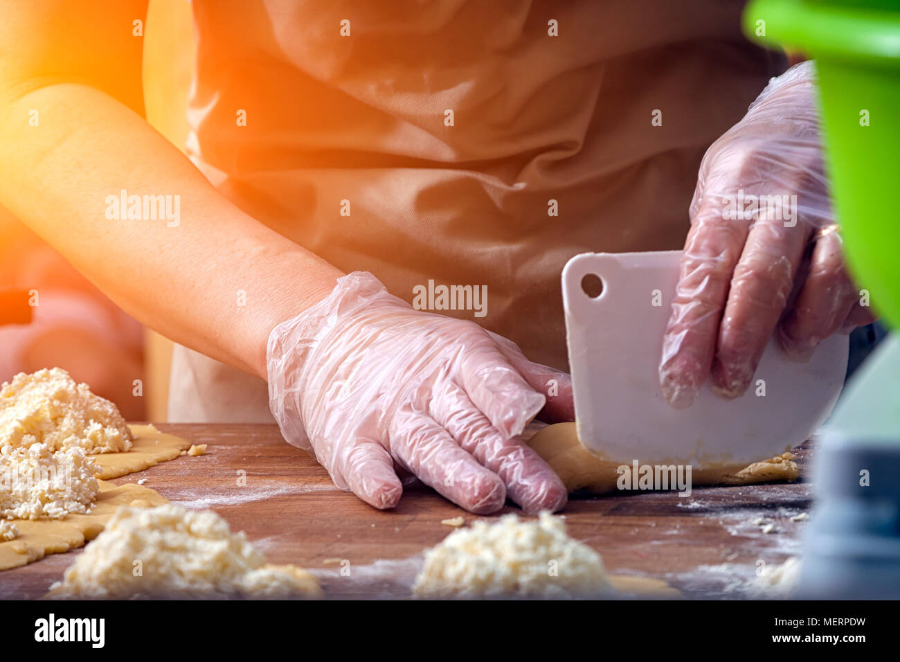 A close-up of a baker in a poor apron sculpts a hot dog bun on a wooden ...