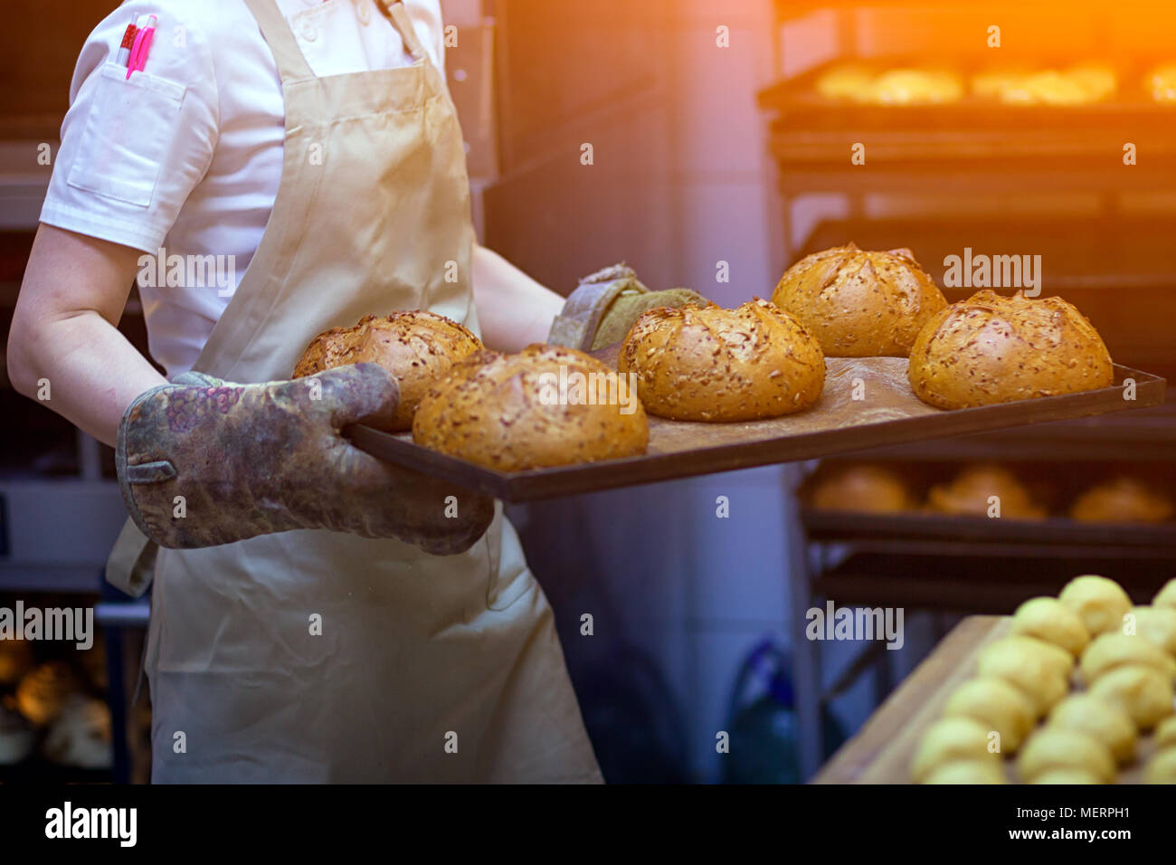 A male baker in white uniform and a beige apron takes bread from an ...
