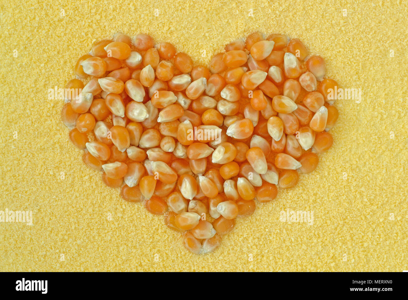 Corn kernels heart on maize flour background Stock Photo - Alamy