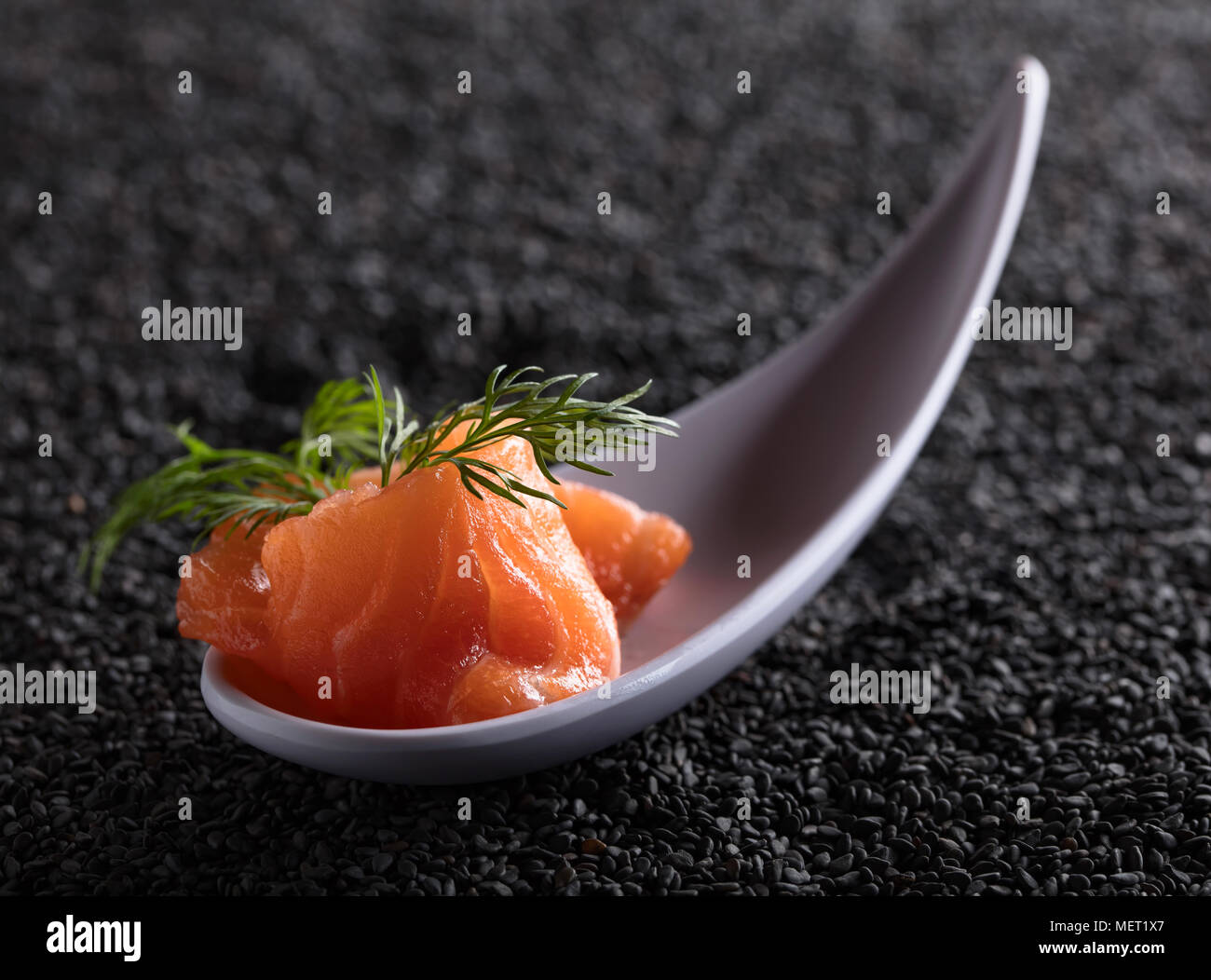 Slice of salted salmon with dill on the background of black sesame ...