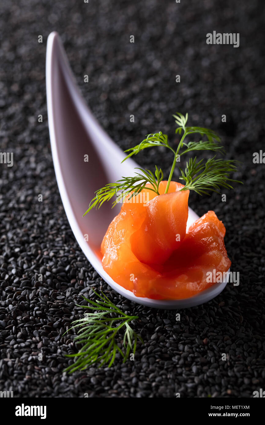 Slice of salted salmon with dill on the background of black sesame ...