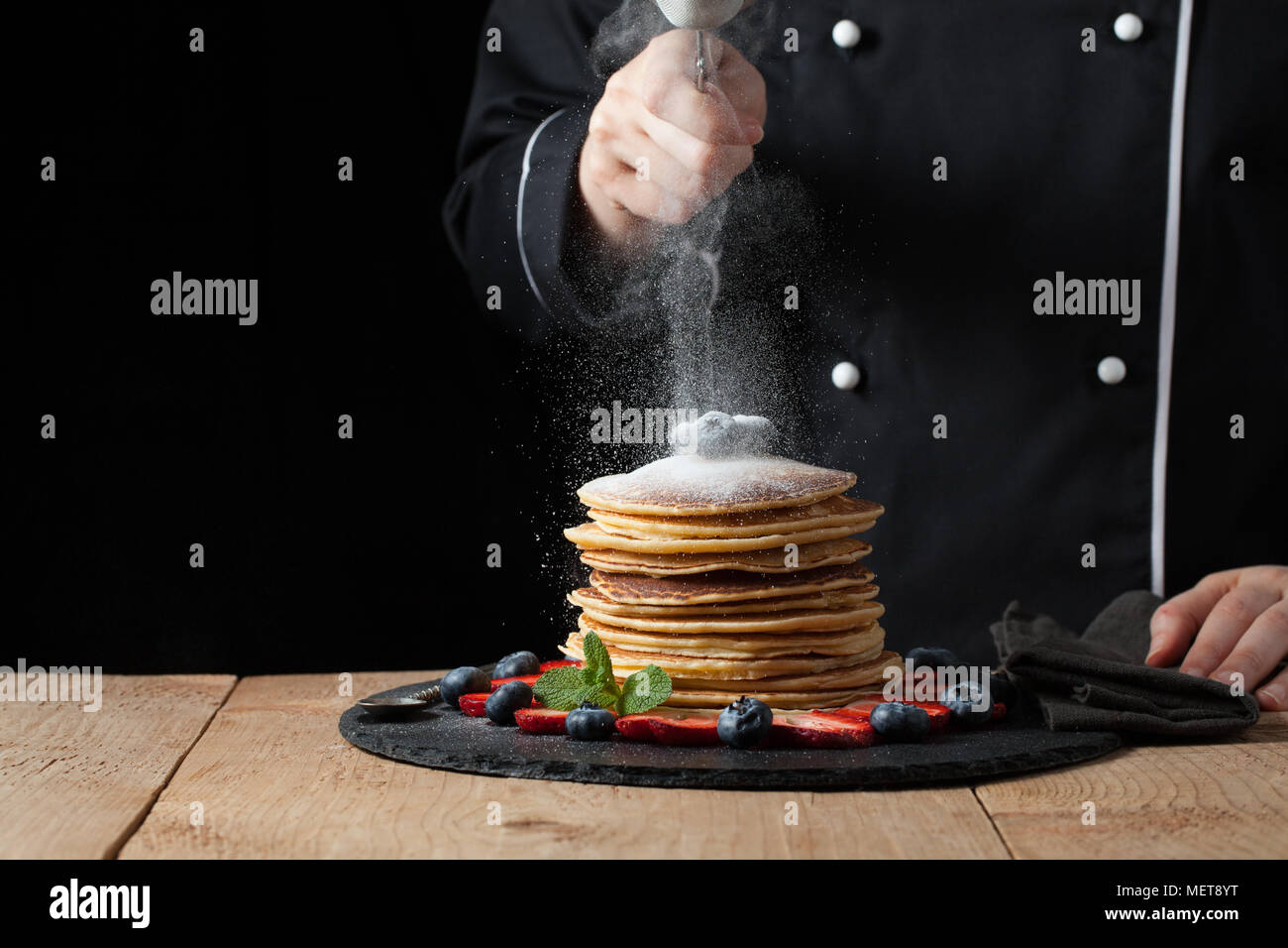 Serving pancakes with powdered sugar and berries. Chef woman hand ...