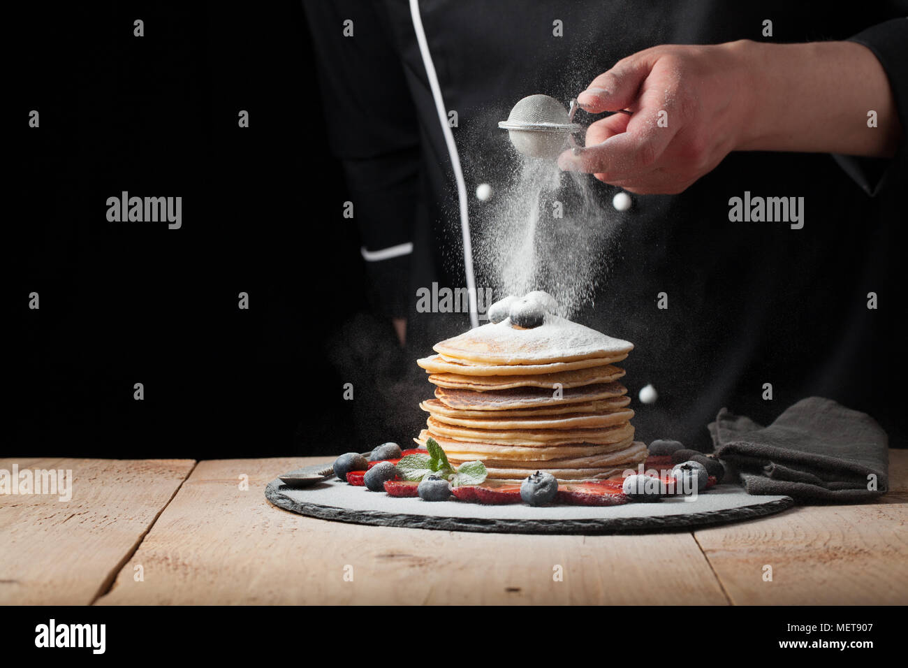 Serving pancakes with powdered sugar and berries. Chef man hand ...
