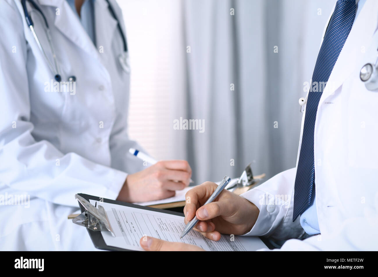 Two unknown doctors filling up medical form on clipboard, just hands ...