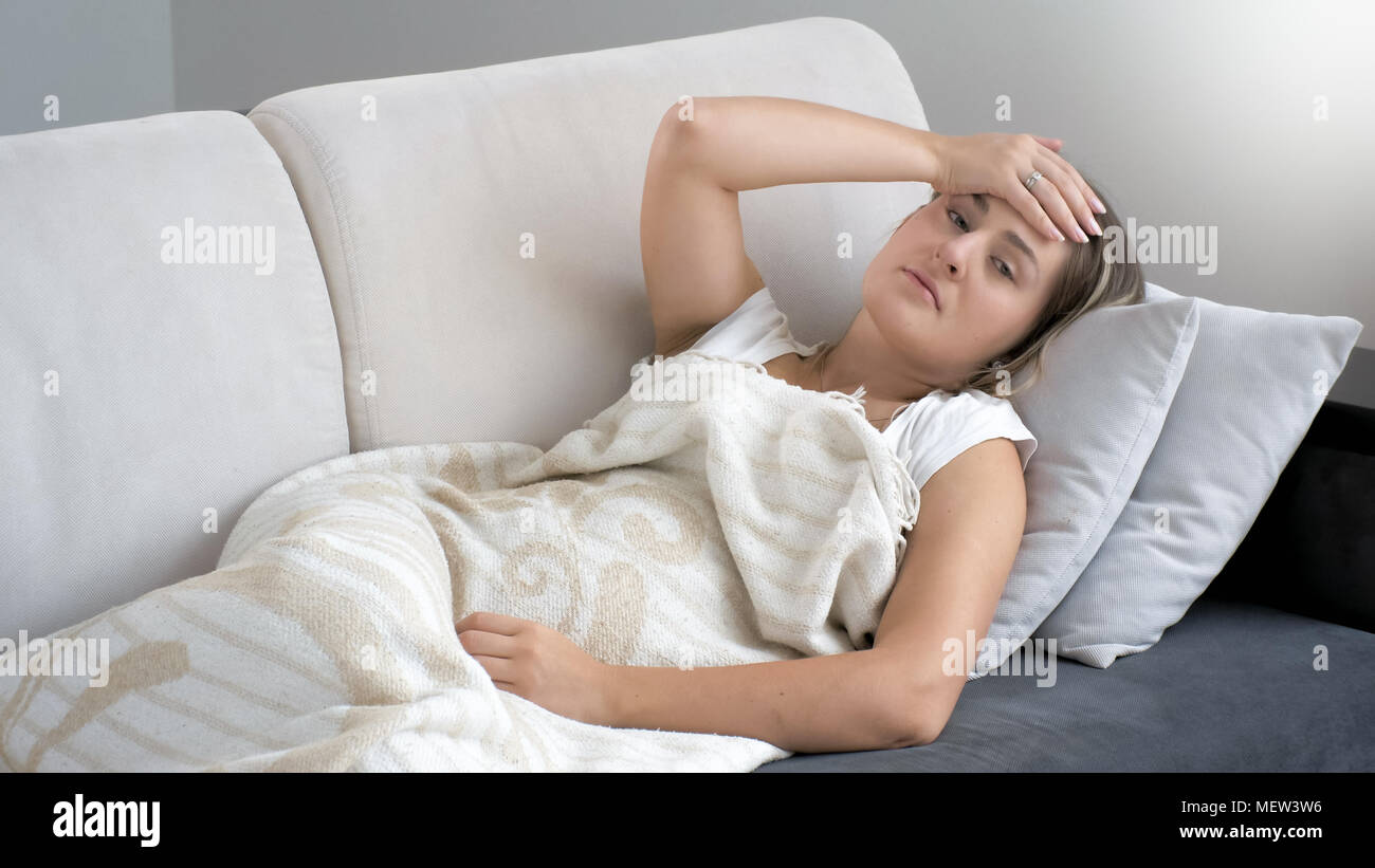Portrait of young woman lying on sofa and feeling high temperature ...
