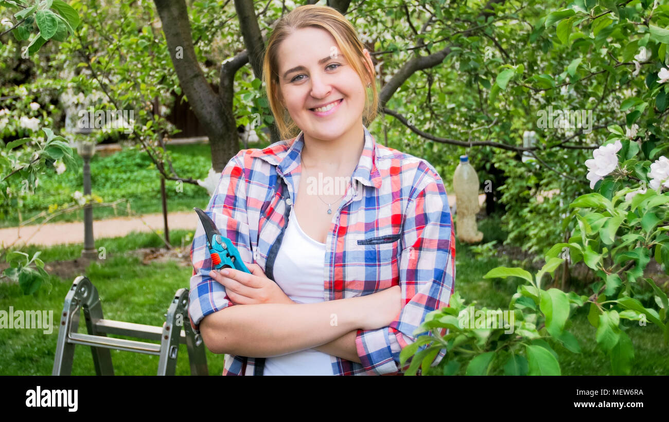 Beautiful smiling woman holding pruner looking in camera at orchard ...