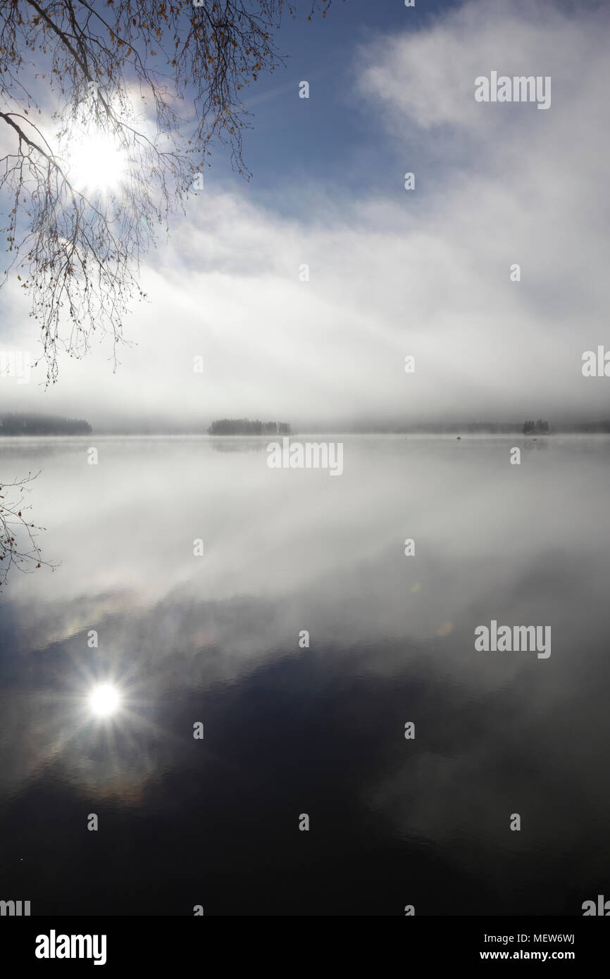 The rising sun is shining through mist rising from a lake in autumn ...