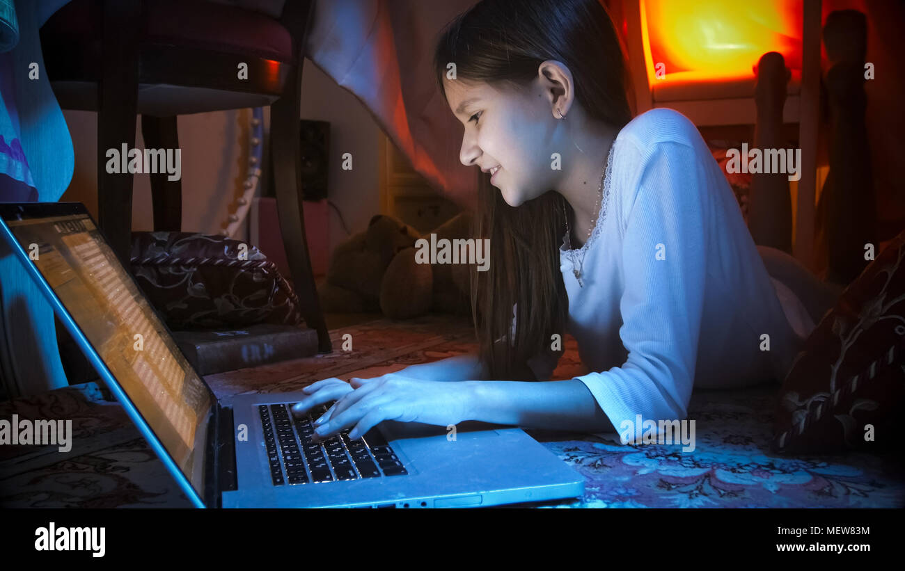Portrait of smiling girl in pajamas lying on floor and typing message ...