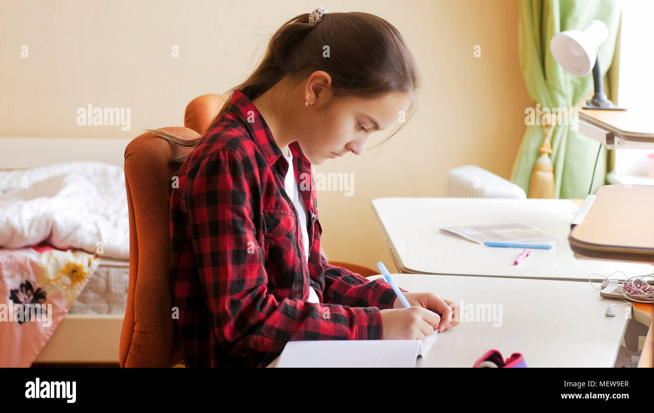 Portrait of beautiful girl writing in copybook behind desk at bedroom ...