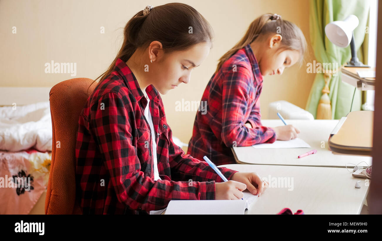 Two teenage girls sitting at big window and doing homework Stock Photo ...