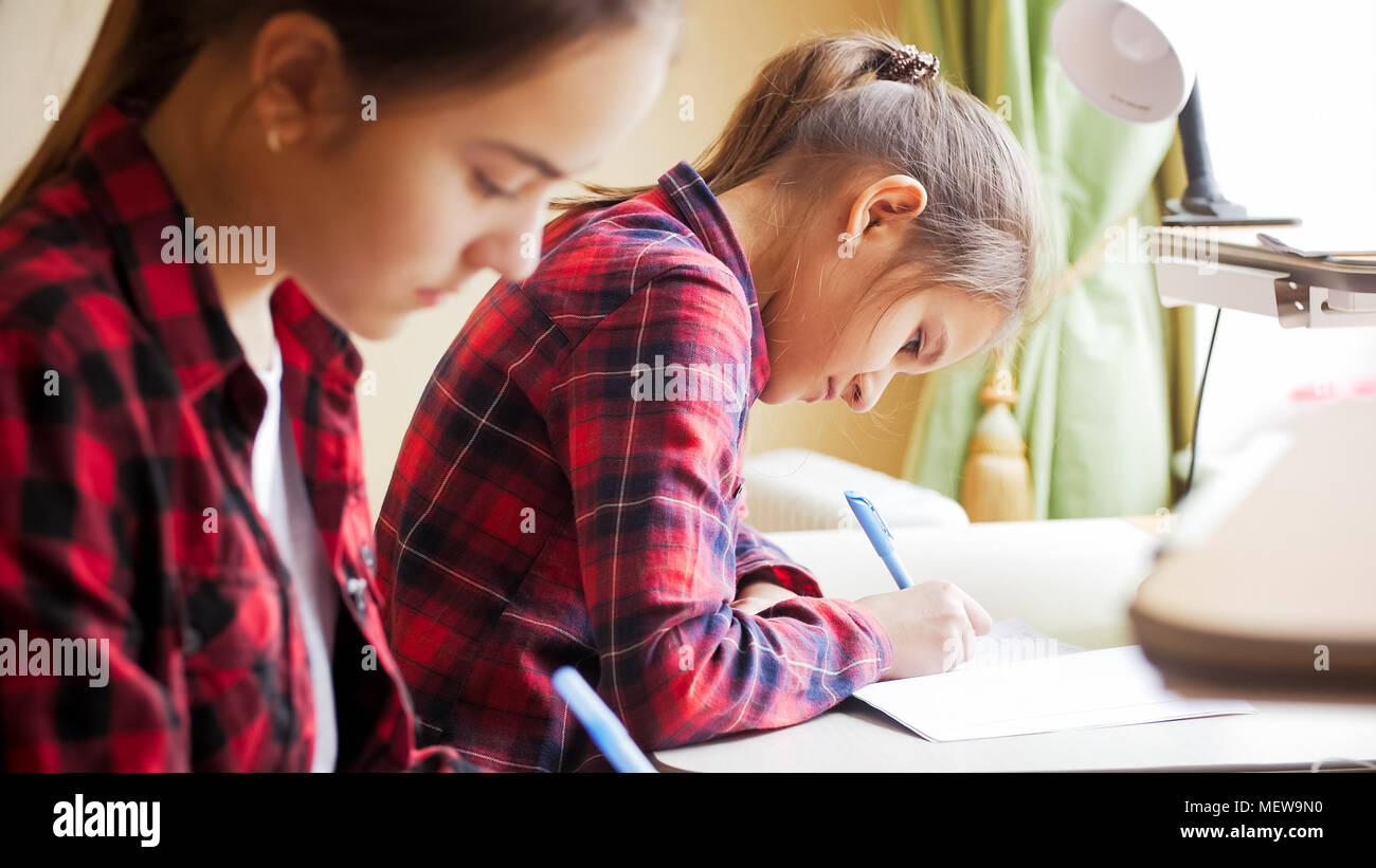 Portrait of two girls sitting behind desk in bedroom and writing ...