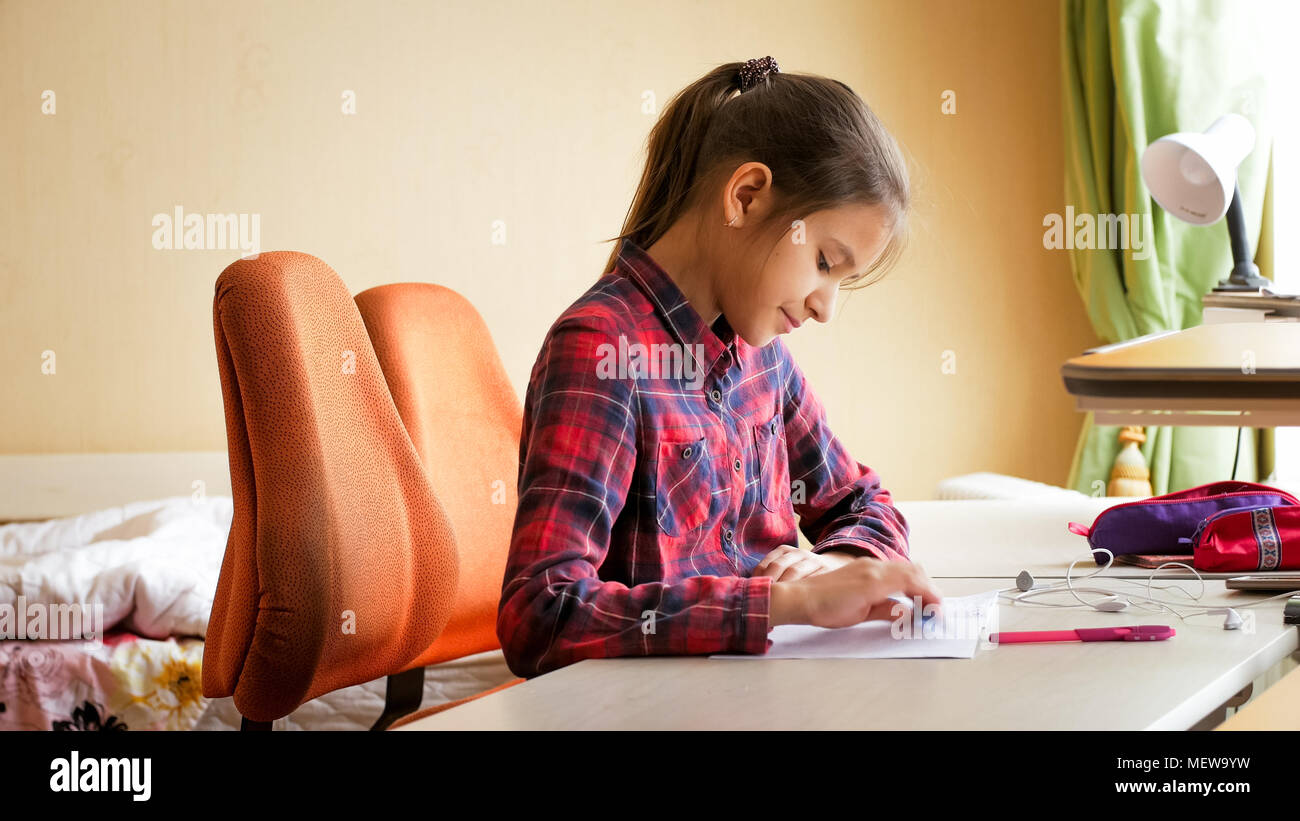 Portrait of teenage girl sitting in bedroom and doing homework behind ...