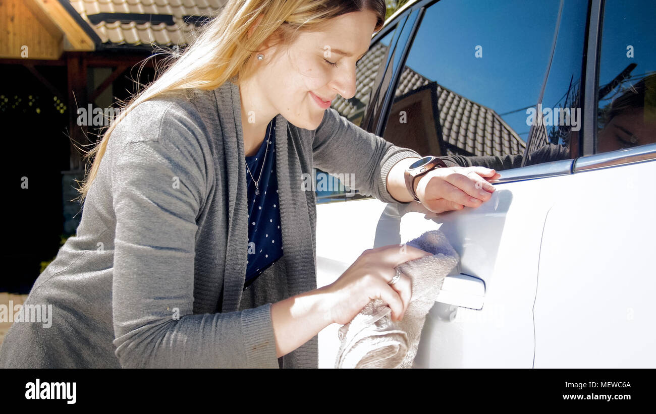 Young smiling female driver taking care of care and clening it with ...