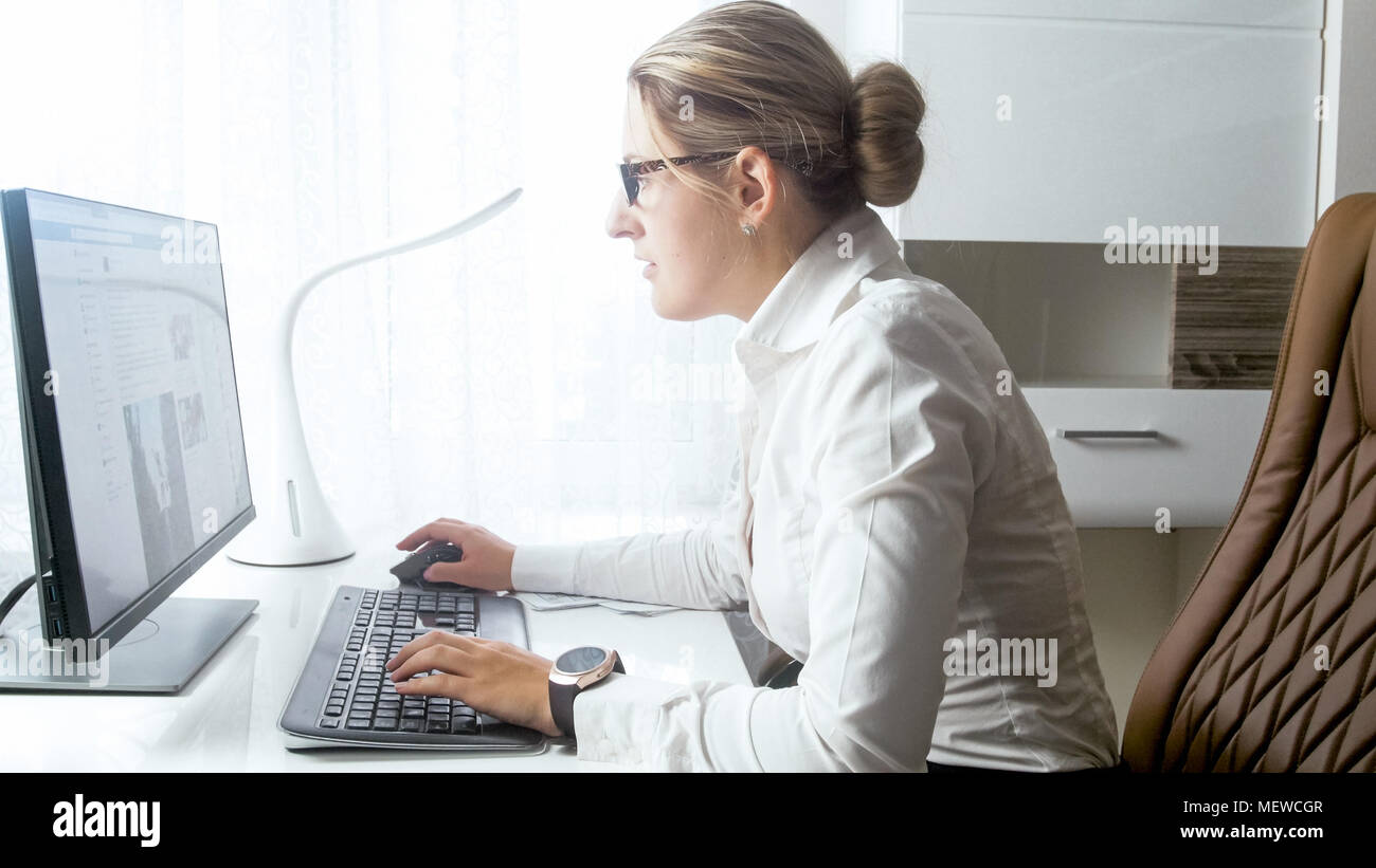 Beautiful young woman sitting behind desk and using computer Stock ...