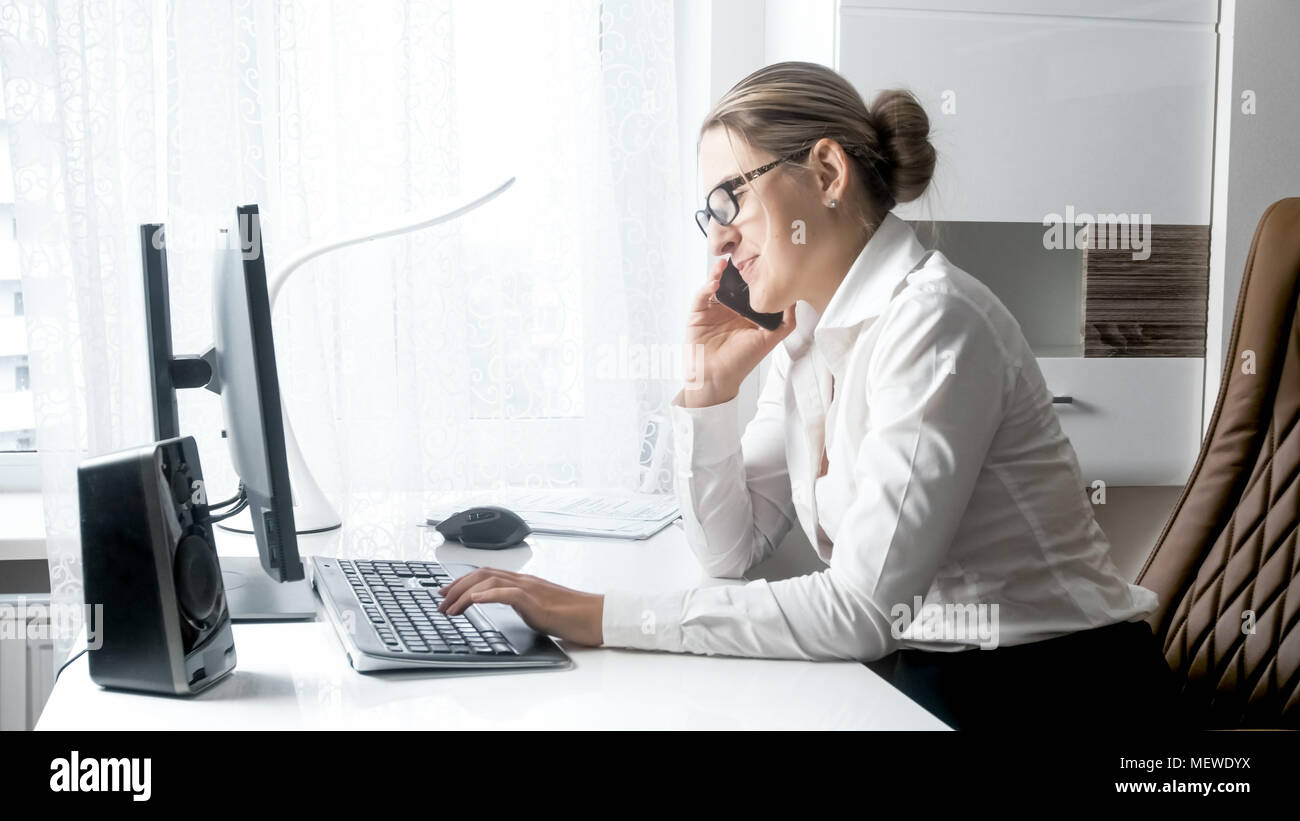 Portrait of young female boss sitting behind desk and talking by phone ...