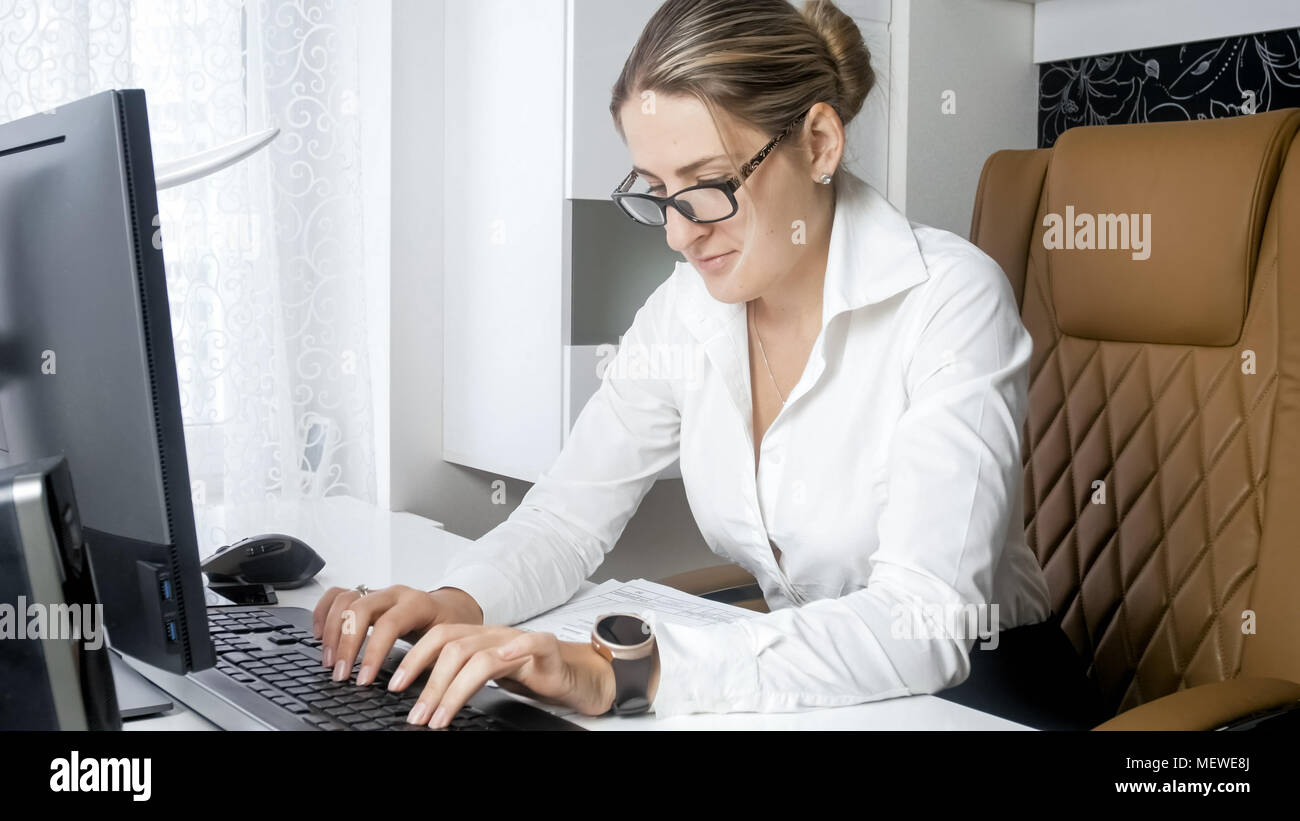 Portrait of concentrated young woman typing text on computer in office ...