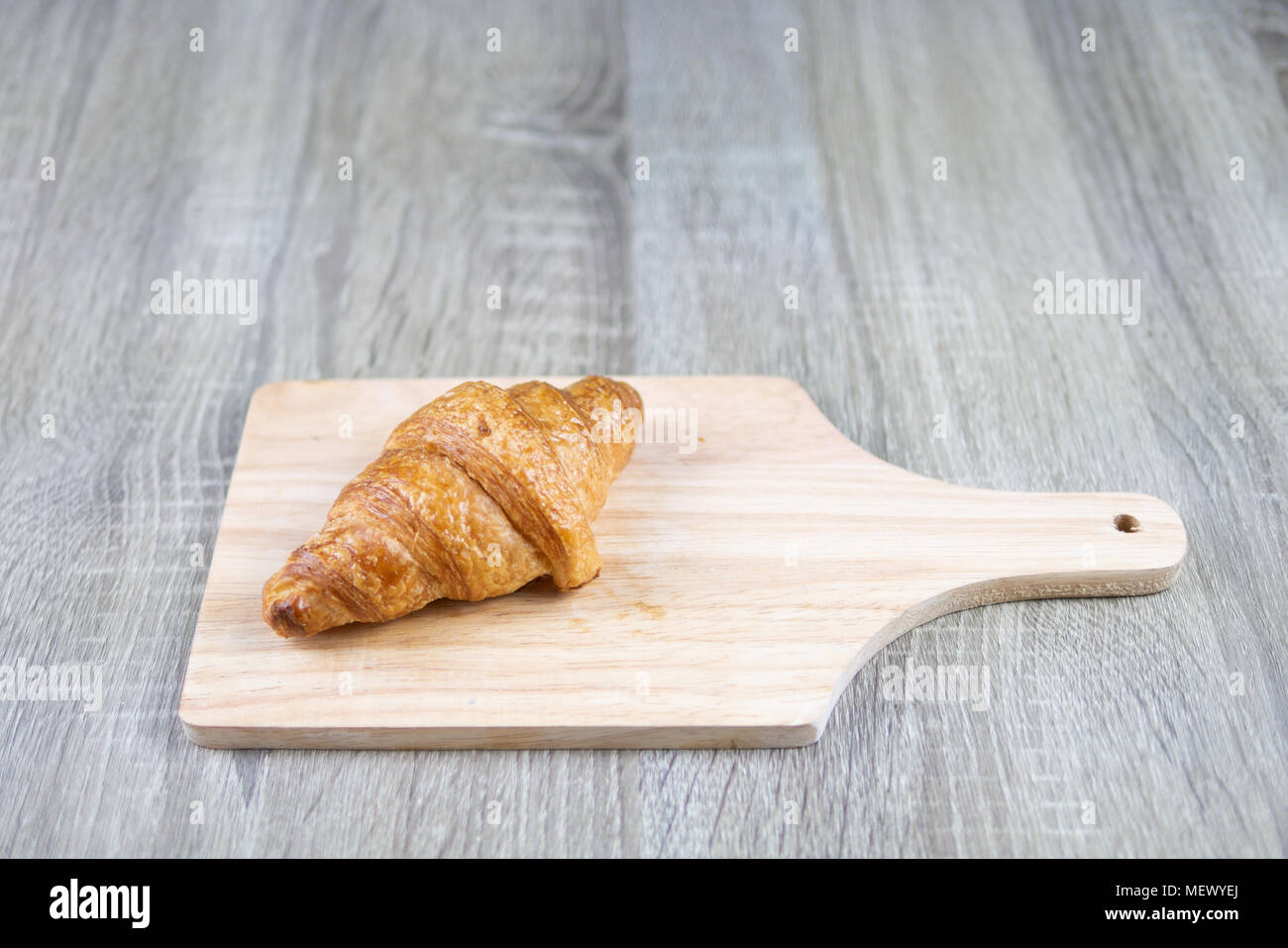 One piece of croissant is placed on a wooden cutting board and table on ...
