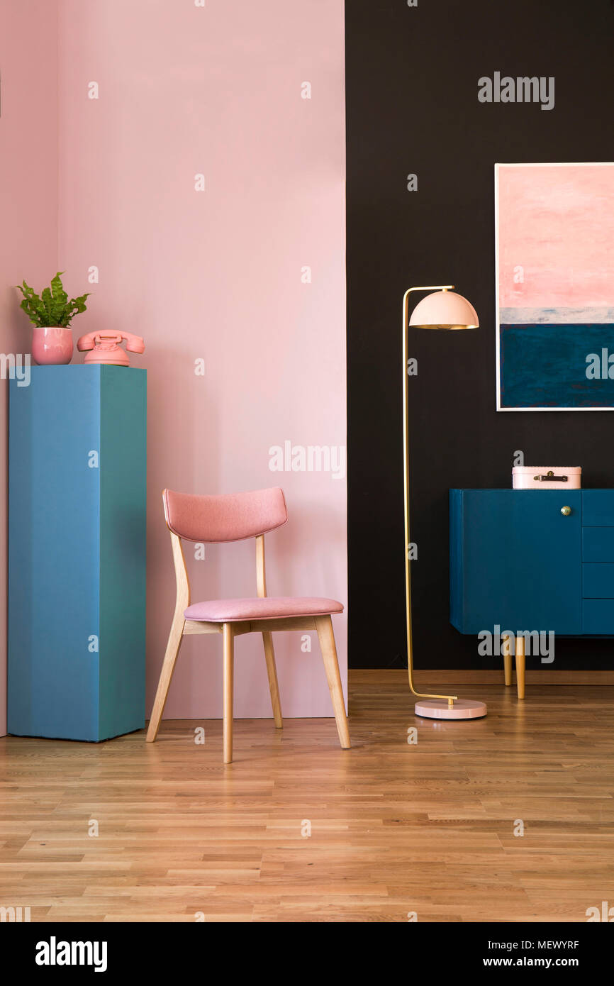 Pink chair, blue stand and lamp set on a pink and black wall in a ...