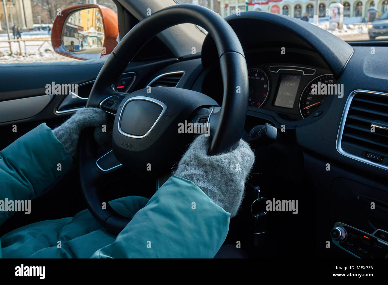 Female hands in the grey mittens on the steering wheel of expensive car ...