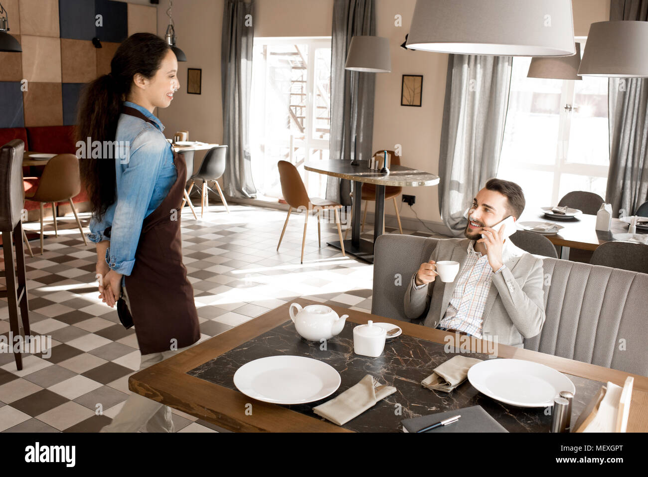 Positive waitress coming to customers table Stock Photo - Alamy
