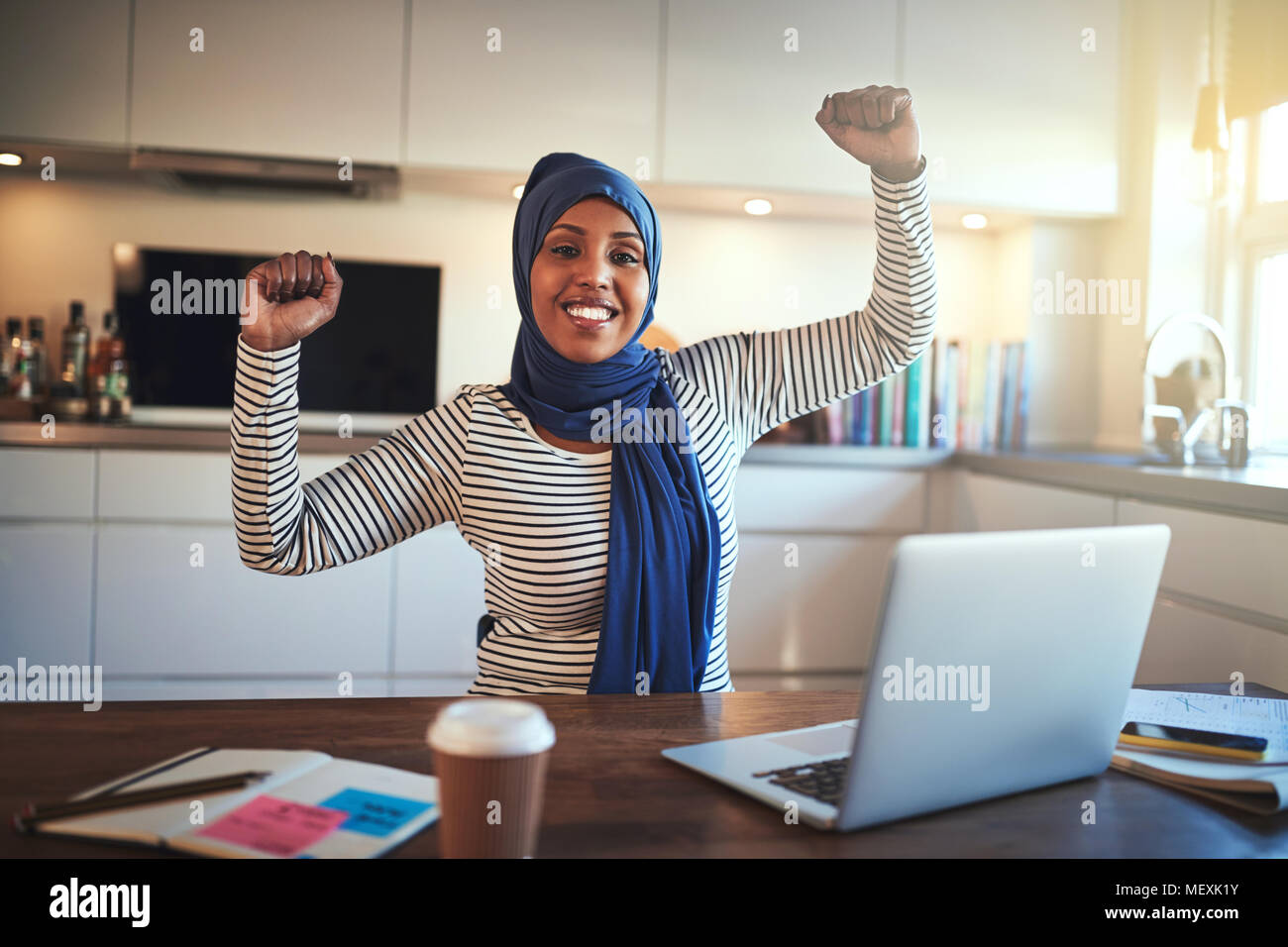 Young Muslim female entrepreneur wearing a hijab raising her arms and ...