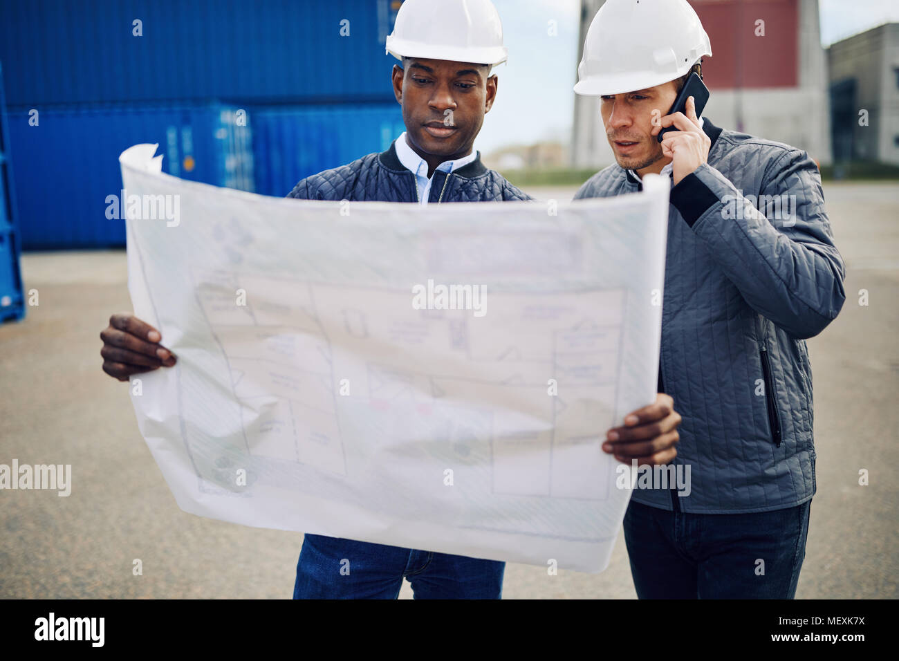 Two engineers reading a blueprint and talking on a cellphone while ...