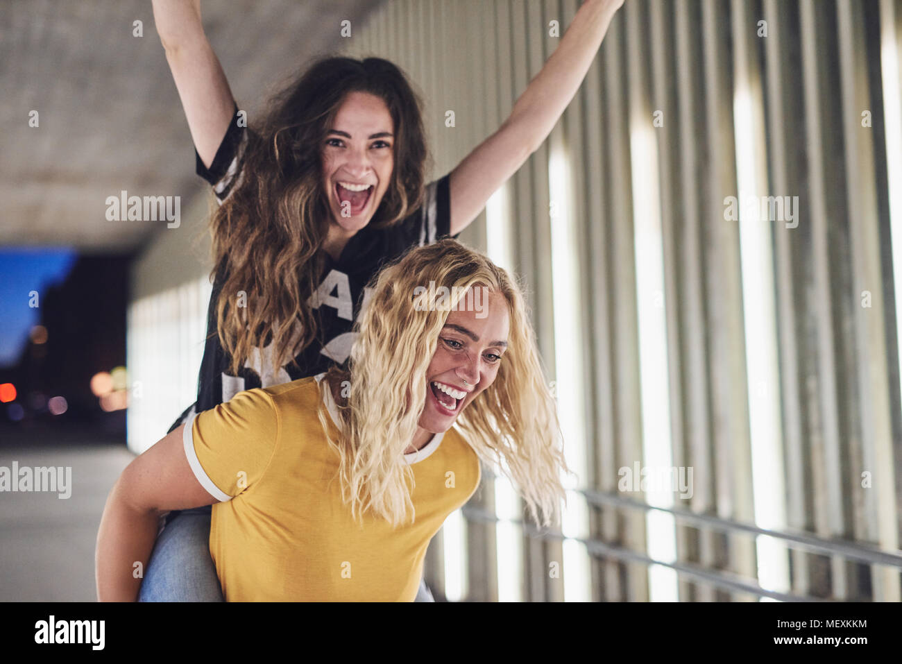 Laughing young woman being carried by her friend while enjoying a night ...