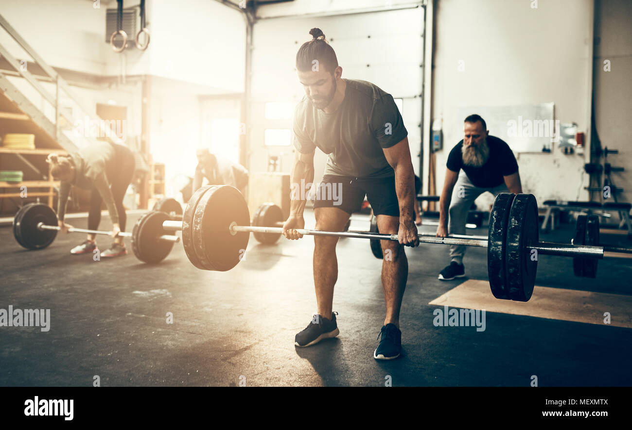 Fit and focused young man in sportswear lifting heavy weights during a ...