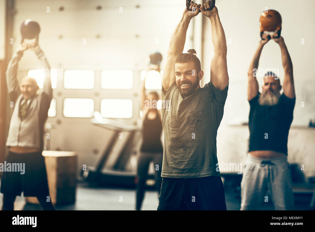 Fit group of people swinging dumbbells over their heads during an ...