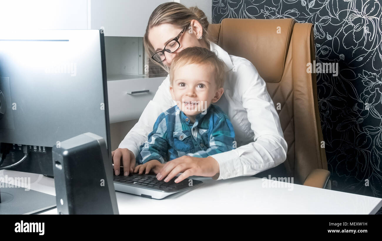 Adorable smiling toddler boy sitting on mothers lap working on computer ...