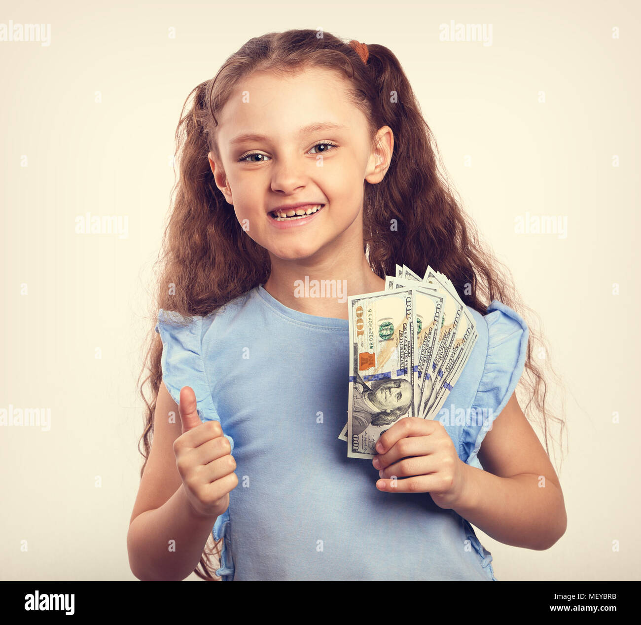 Happy smiling rich kid girl holding money and showing thumb up sign on ...