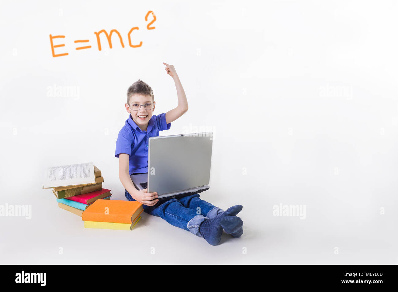 Portrait of cute teen schoolboy sitting near books and typing on laptop ...