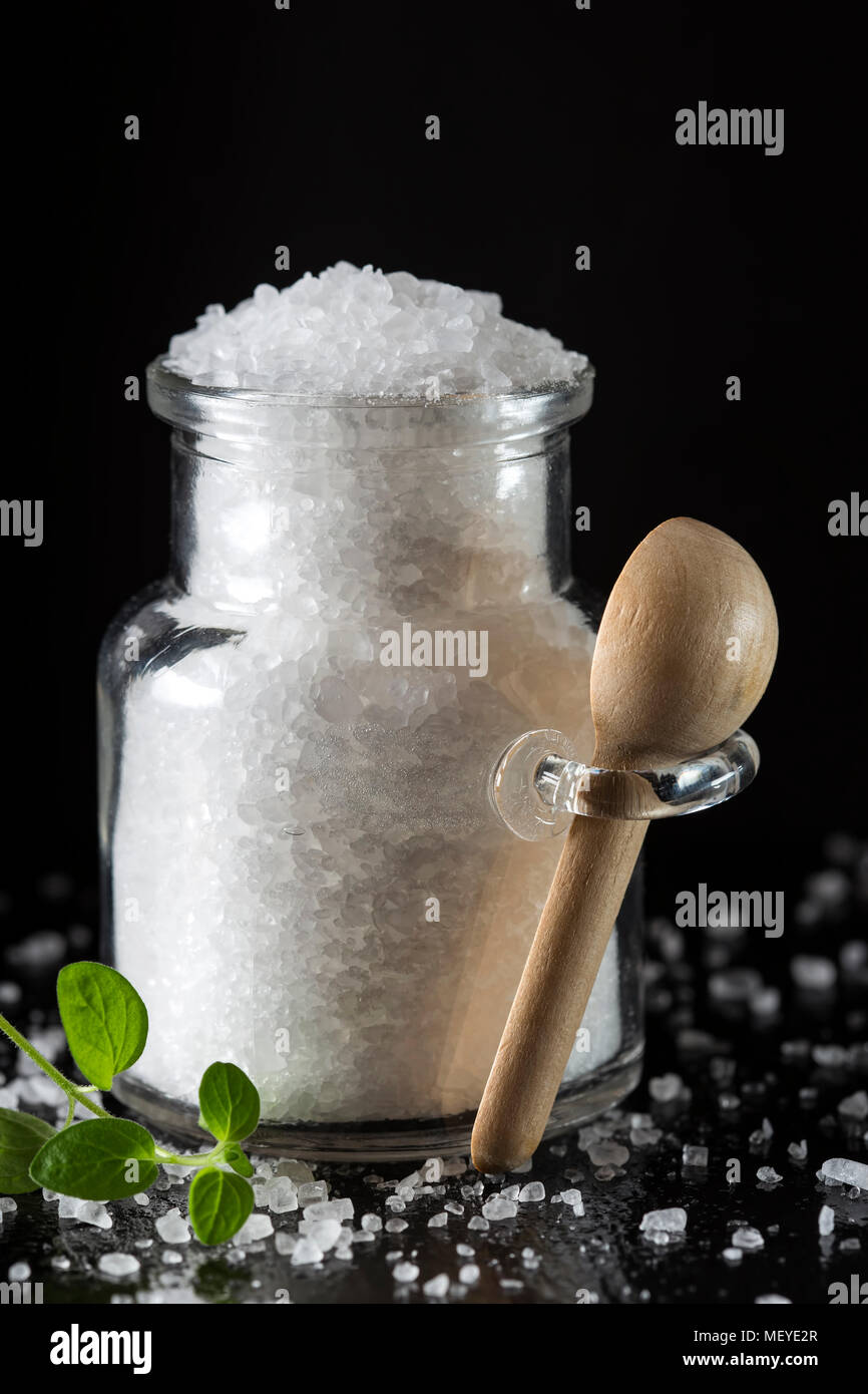 Glass jar filled with sea salt on dark slate background with green ...