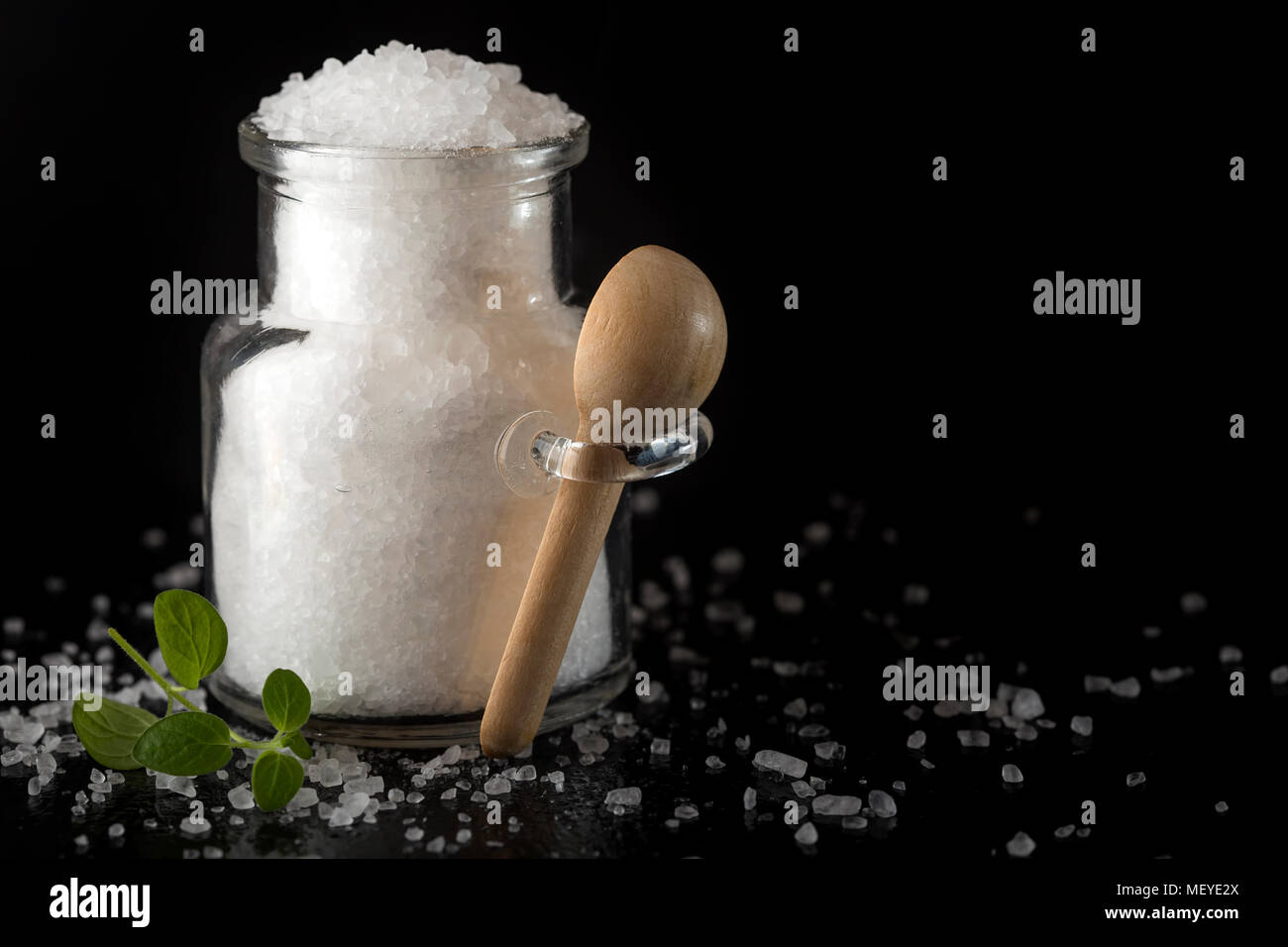 Glass jar filled with sea salt on dark slate background with green ...