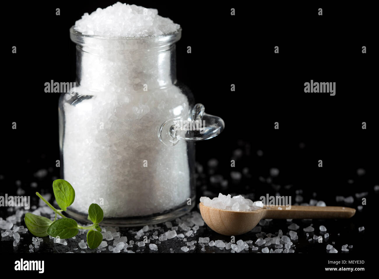 Glass jar filled with sea salt on dark slate background with green ...