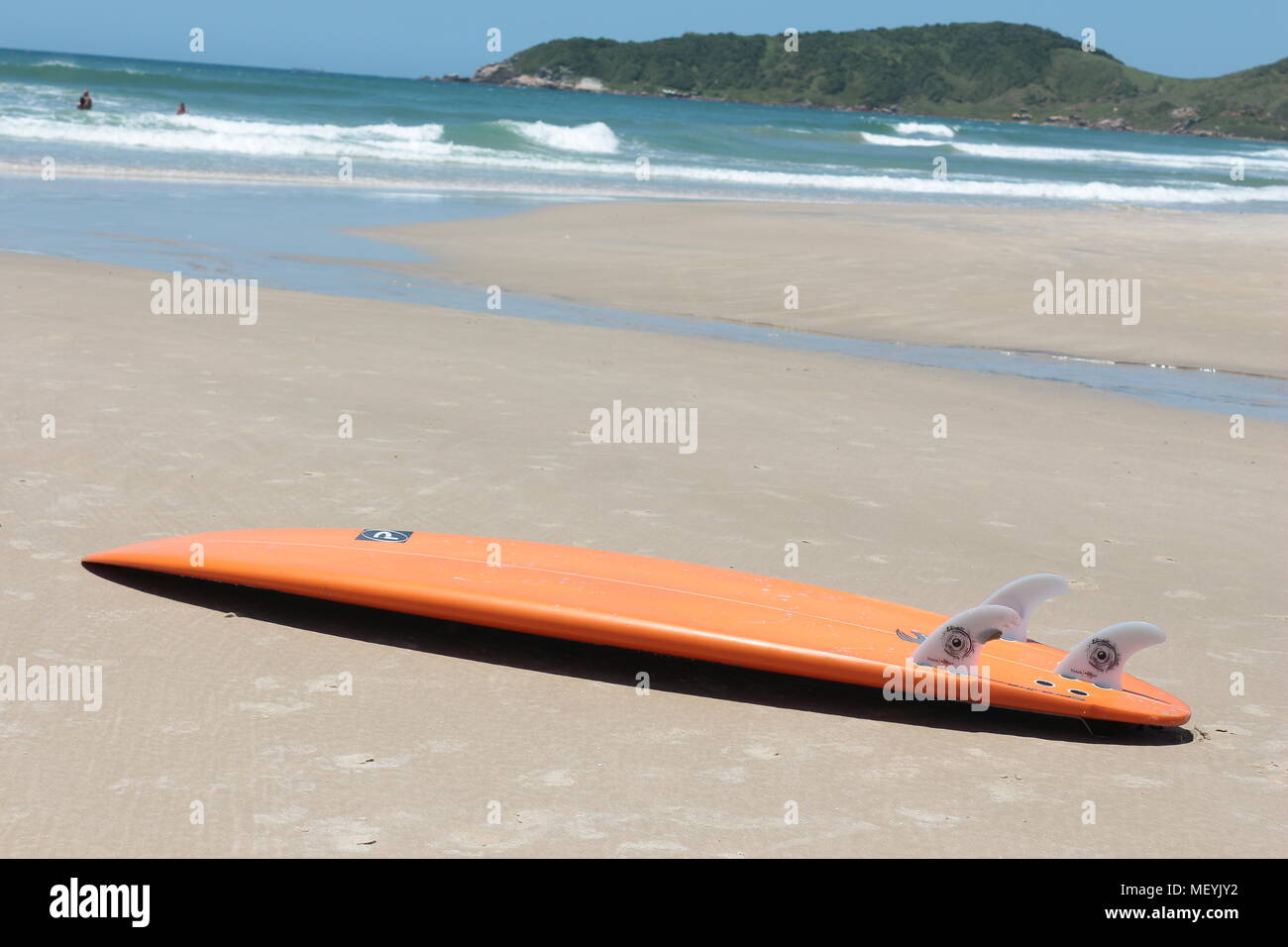 Orange surfing board lying on a sandy beach with the Atlantic Ocean in ...