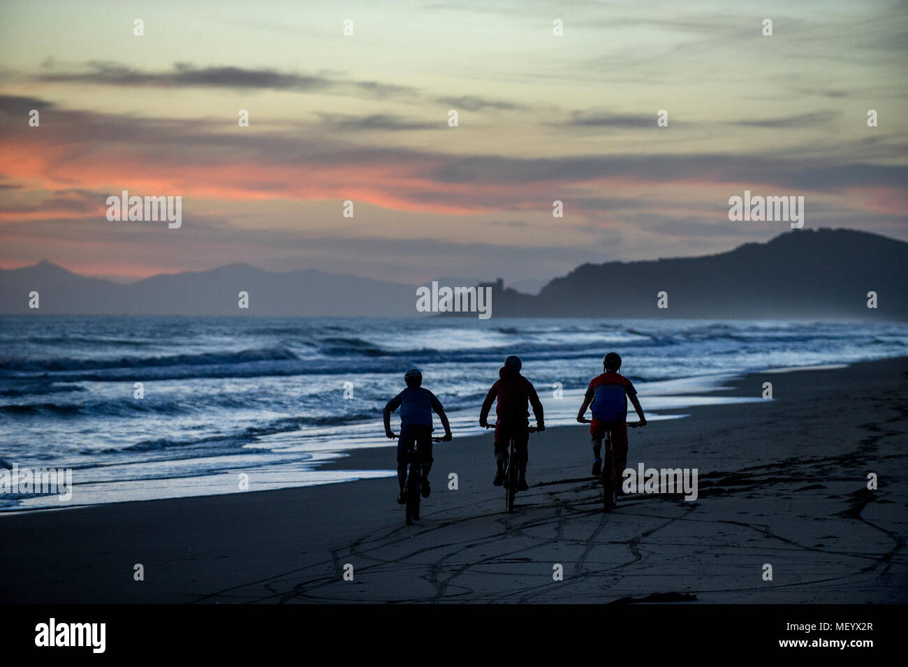 Three mountain bikers ride along a beach near the port of Punta Ala in ...