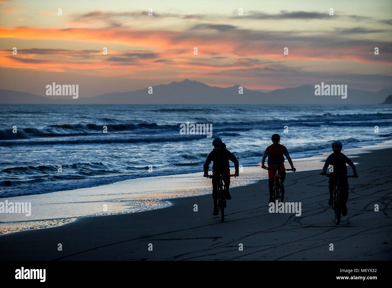 Three mountain bikers ride along a beach near the port of Punta Ala in ...
