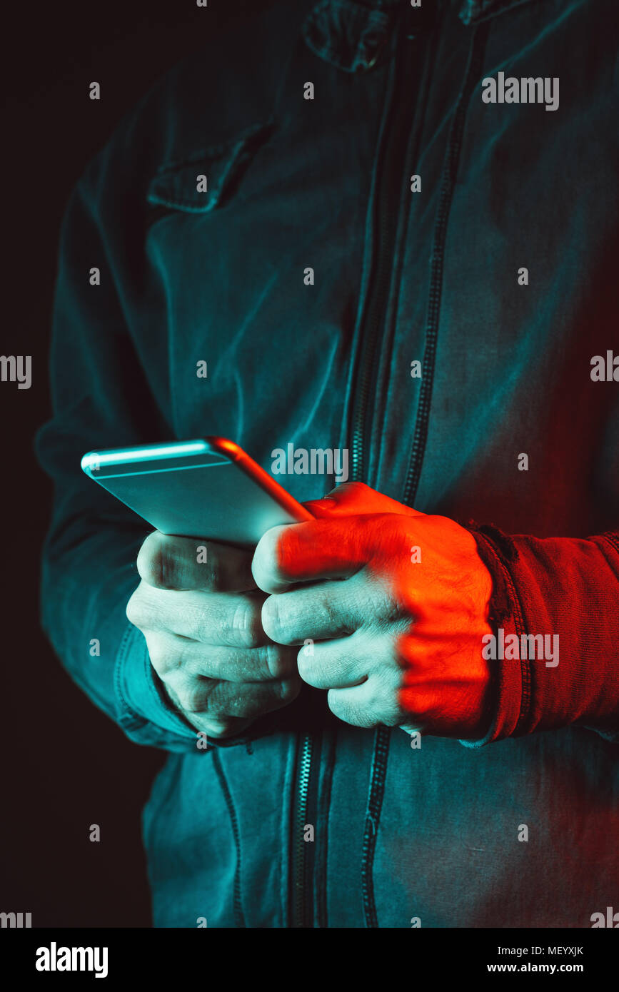 Man using mobile phone, blue and red lit low key cropped close up image ...