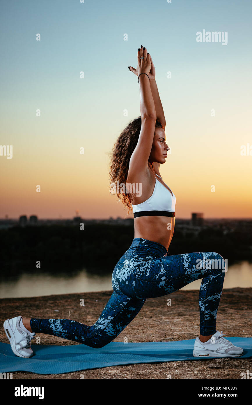 A profile of a young fitness woman doing stretching exercises by the ...