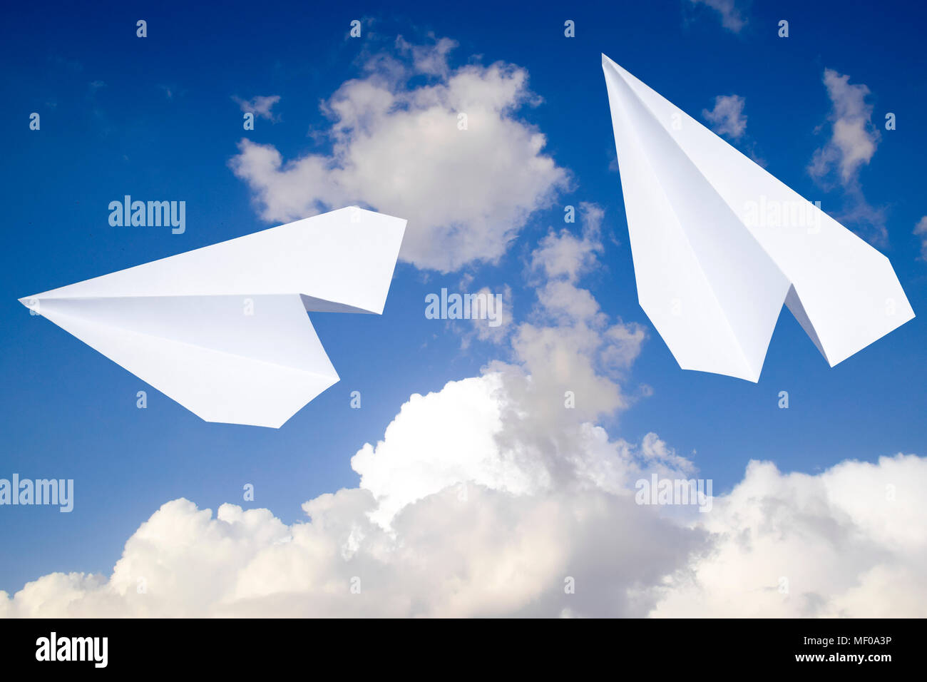 White paper airplane in a blue sky with clouds. The message symbol in ...