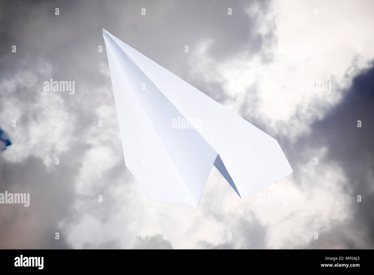 White paper airplane in a blue sky with clouds. The message symbol in ...