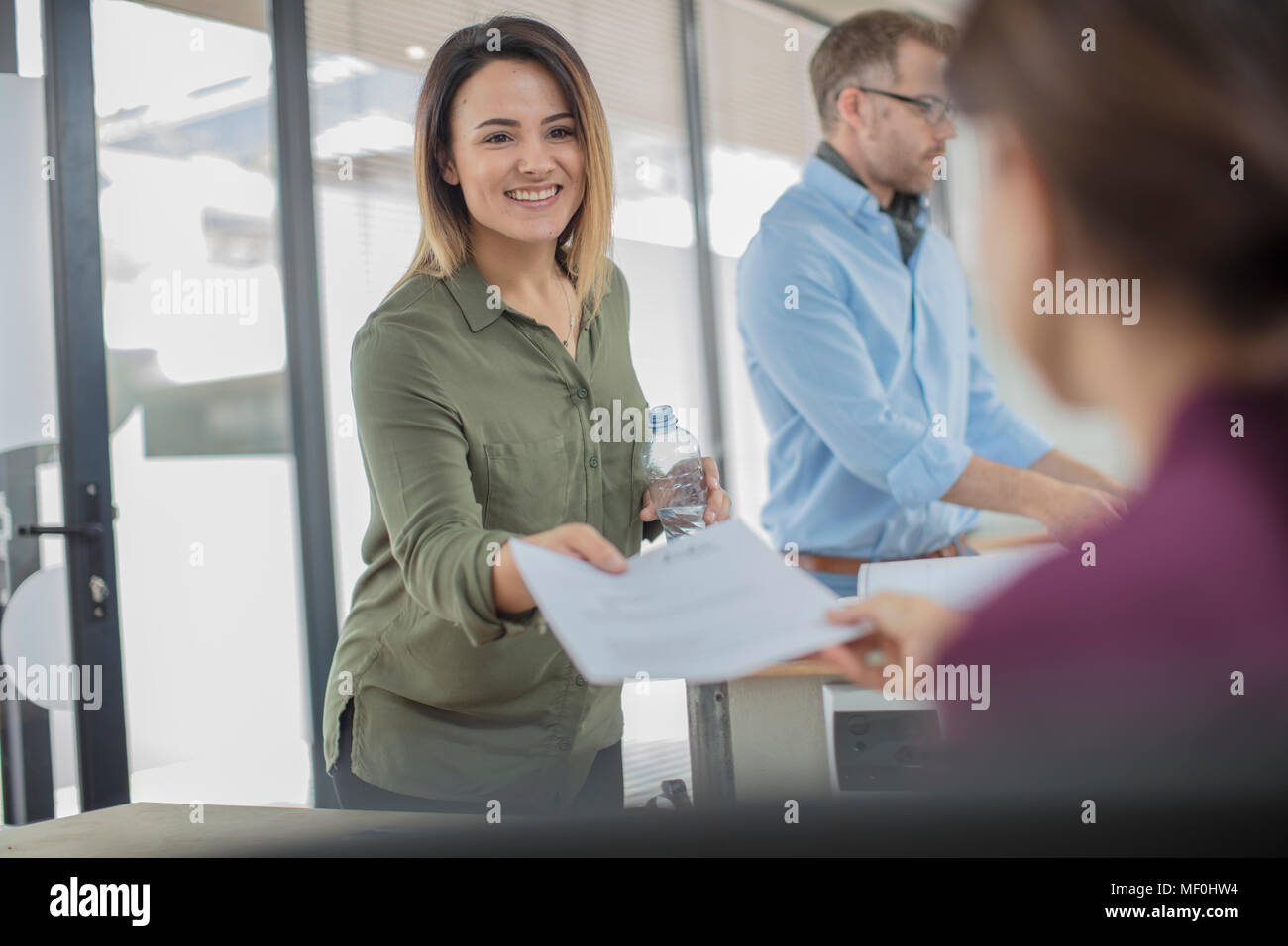 Smiling businesswoman in office handing over paper to colleague Stock ...