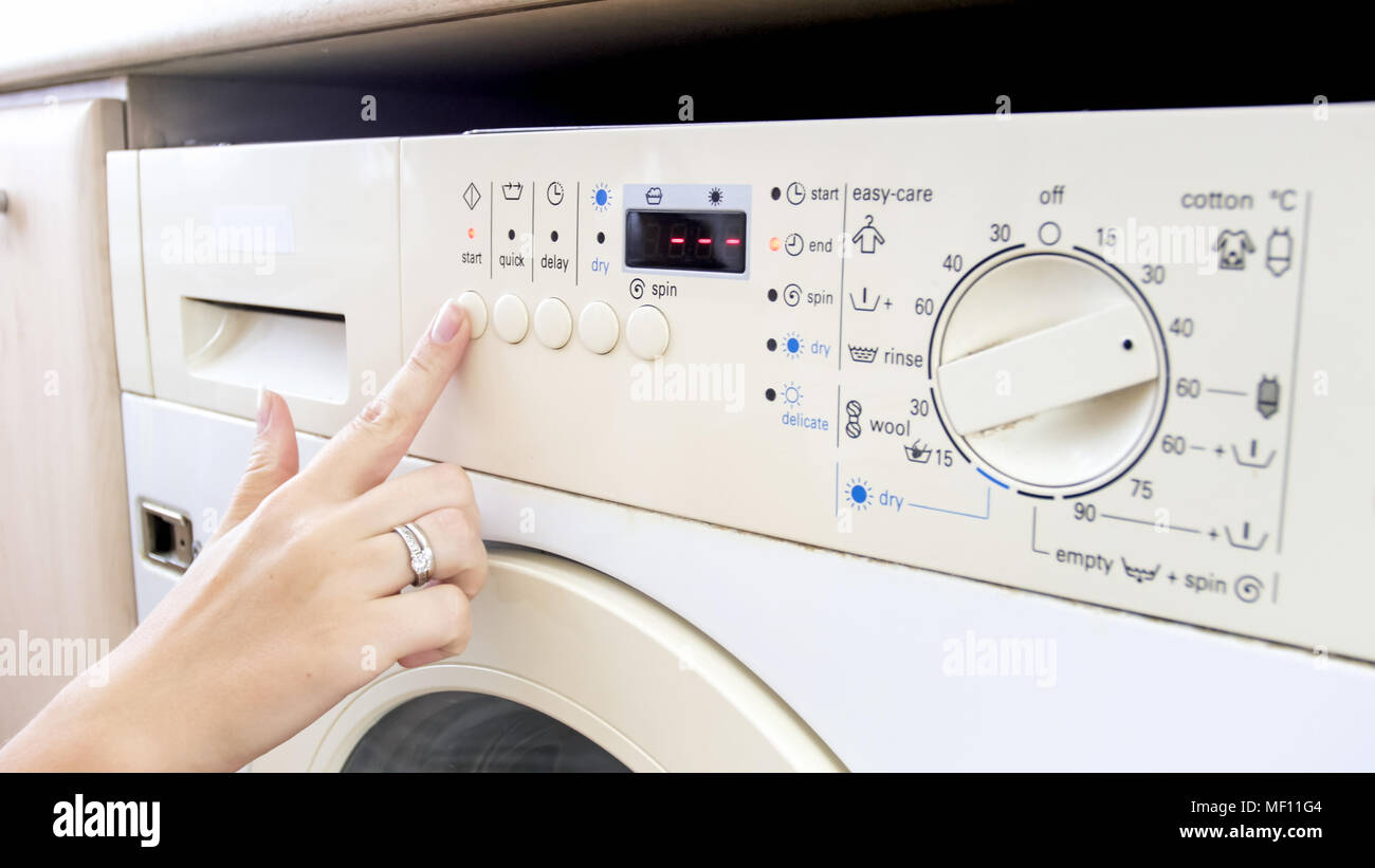 Closeup image of female hand pushing start button on washing machine ...